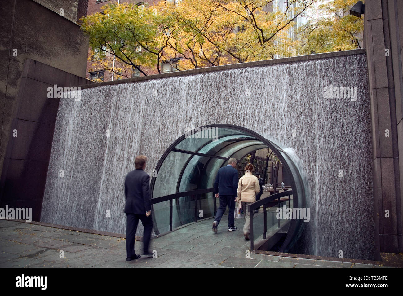 People walking through waterfall covered archway that leads to plaza ...