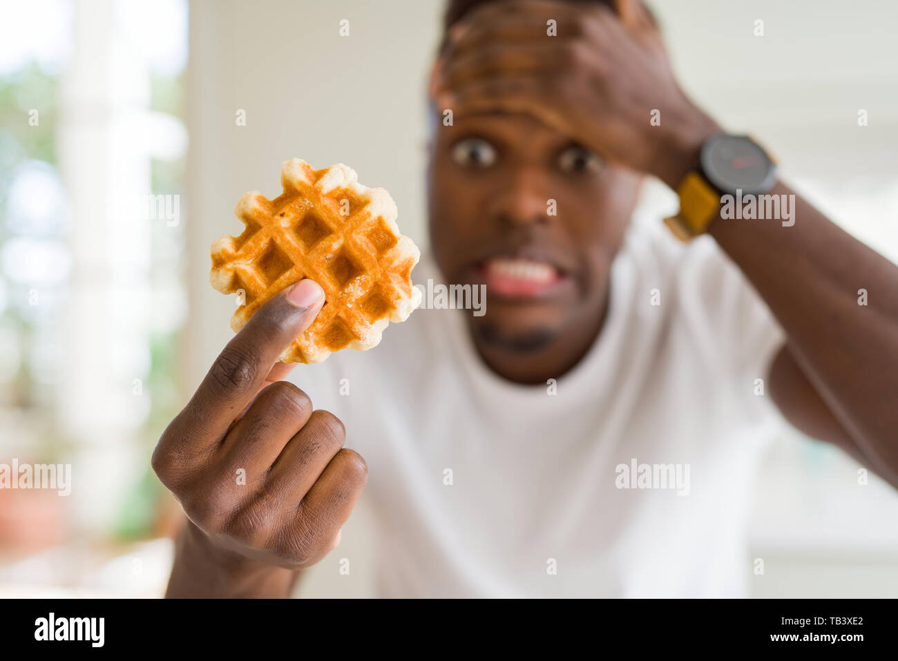 African american man eating sweet Belgian waffle stressed with hand on ...