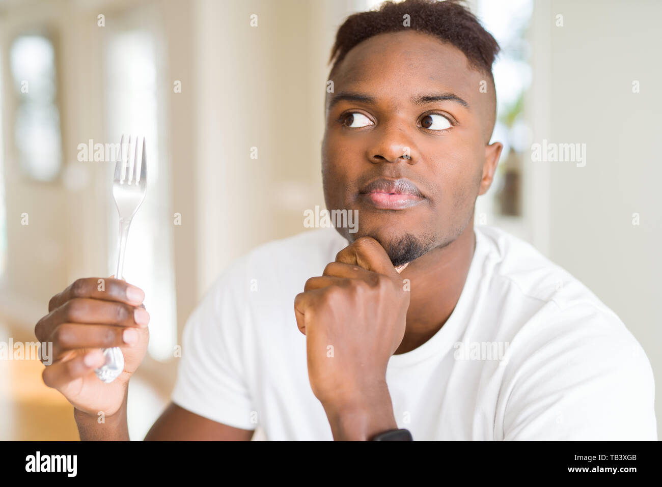 African american man holding silver fork cutlery serious face thinking ...