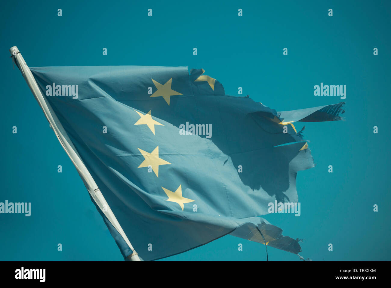Euro skepticism concept. Torn EU flag wave on blue sky. European Union ... Euro skepticism concept. Torn EU flag wave on blue sky. European Union ...