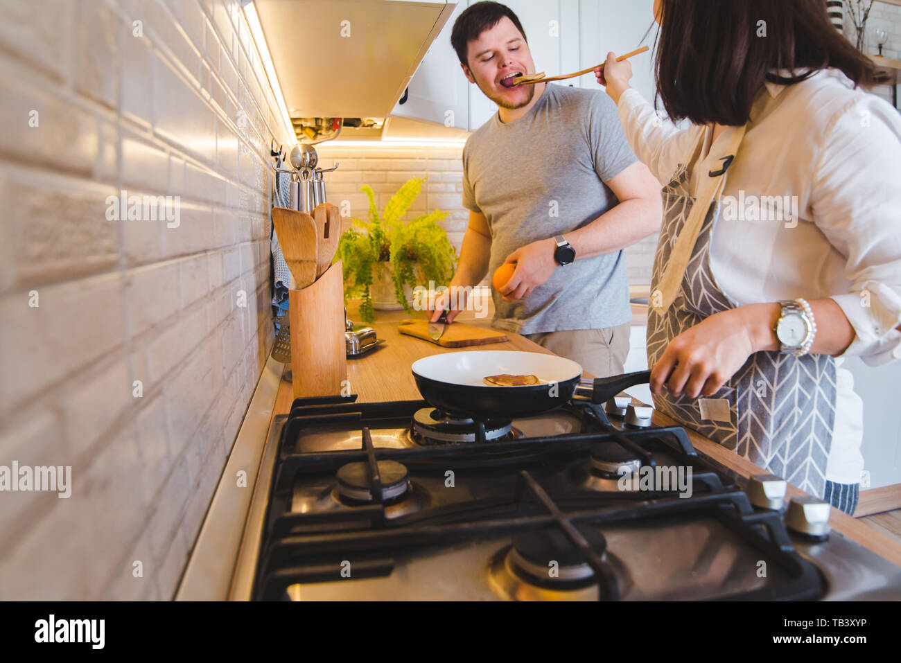 couple cooking together at the kitchen. frying pancakes cutting orange ...