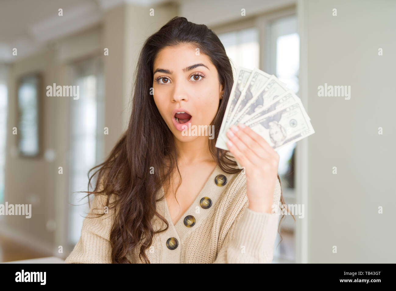 Young woman holding 20 dollars bank notes scared in shock with a ...