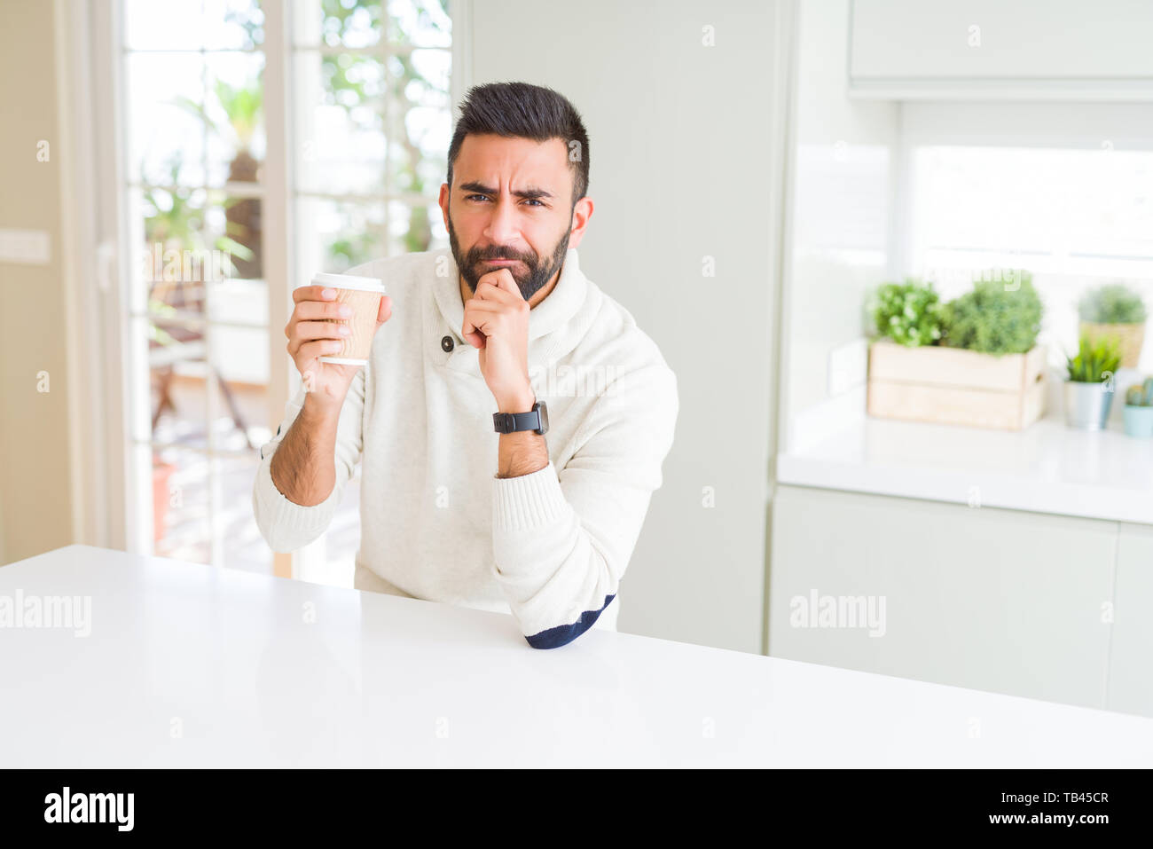 Handsome hispanic man drinking a coffee in a paper cup serious face ...