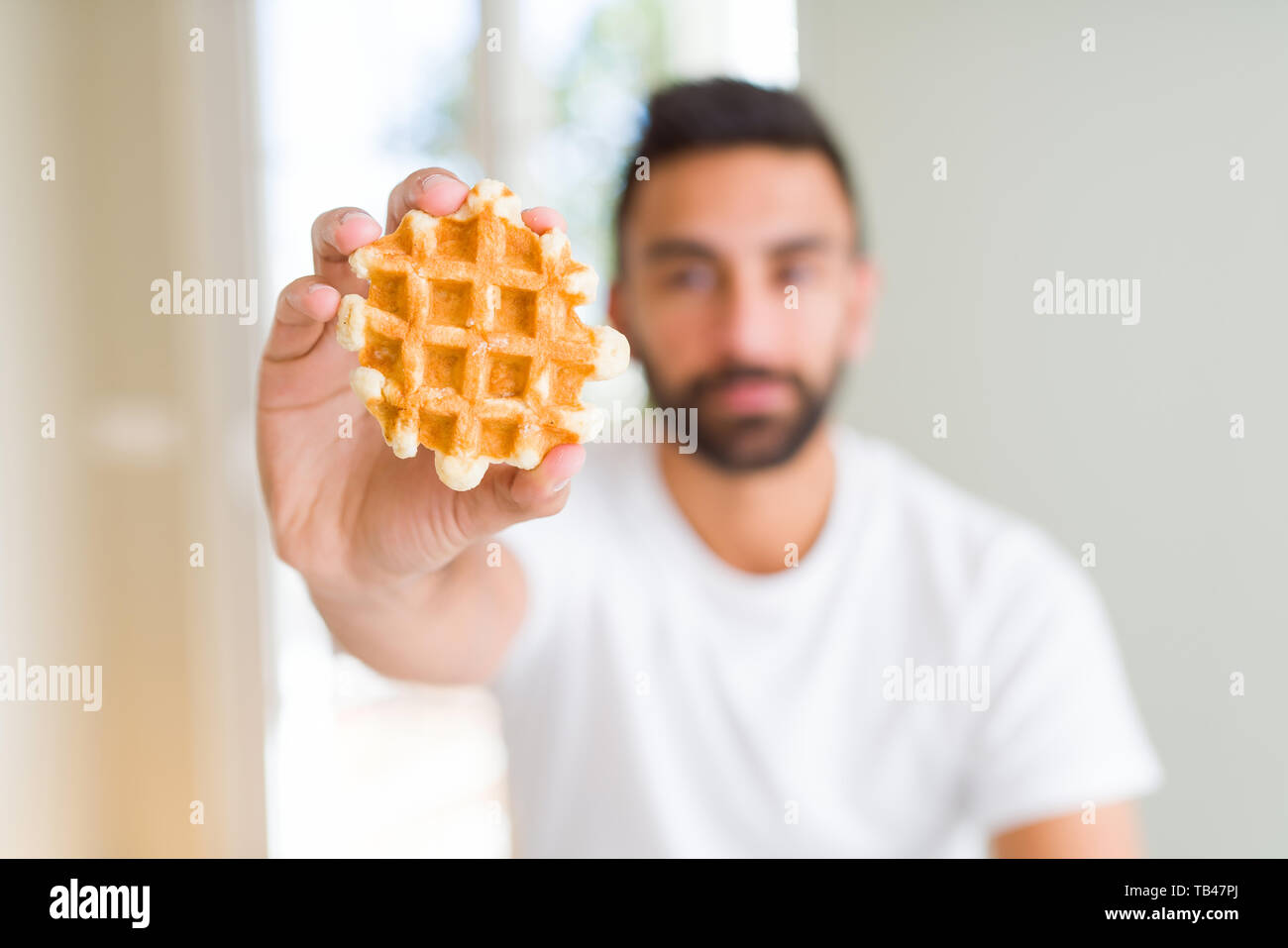 Handsome hispanic man eating sweet belgian waffle pastry with a ...