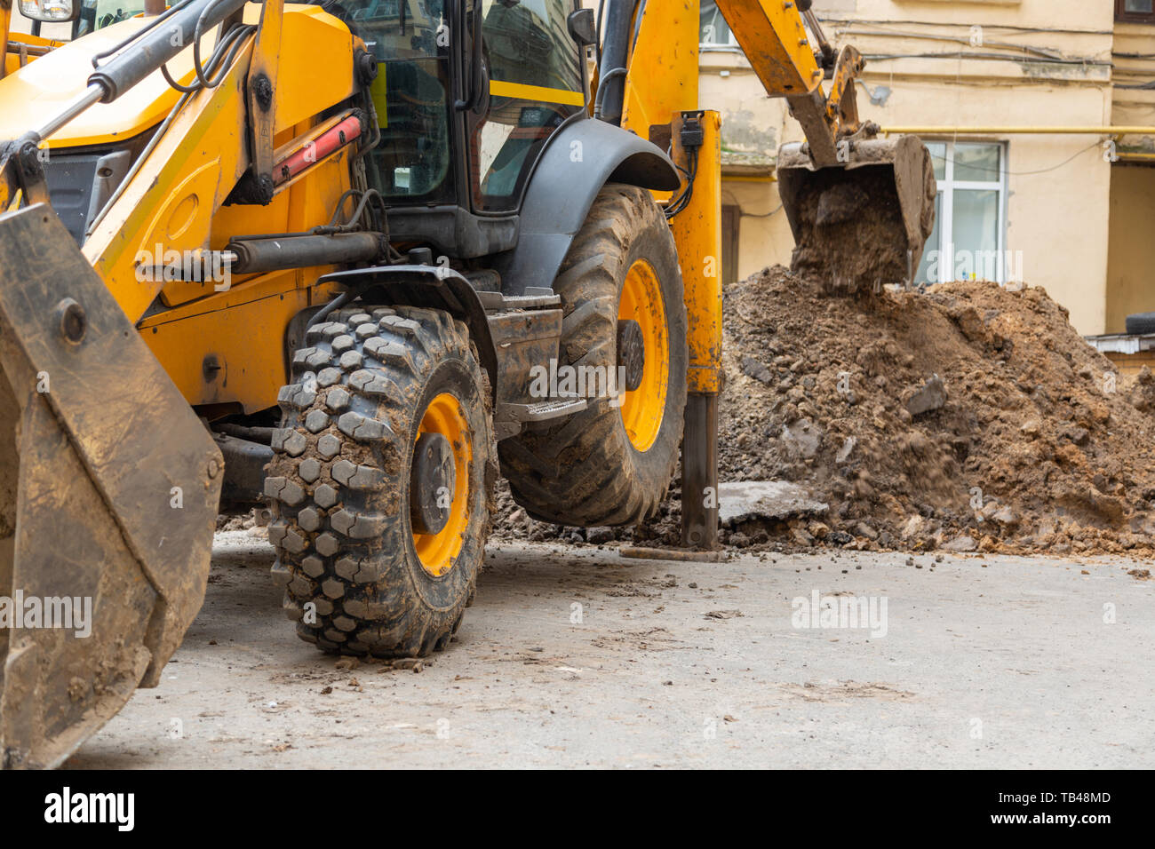 Excavator digs a trench. Repair work in the courtyard of a residential ...