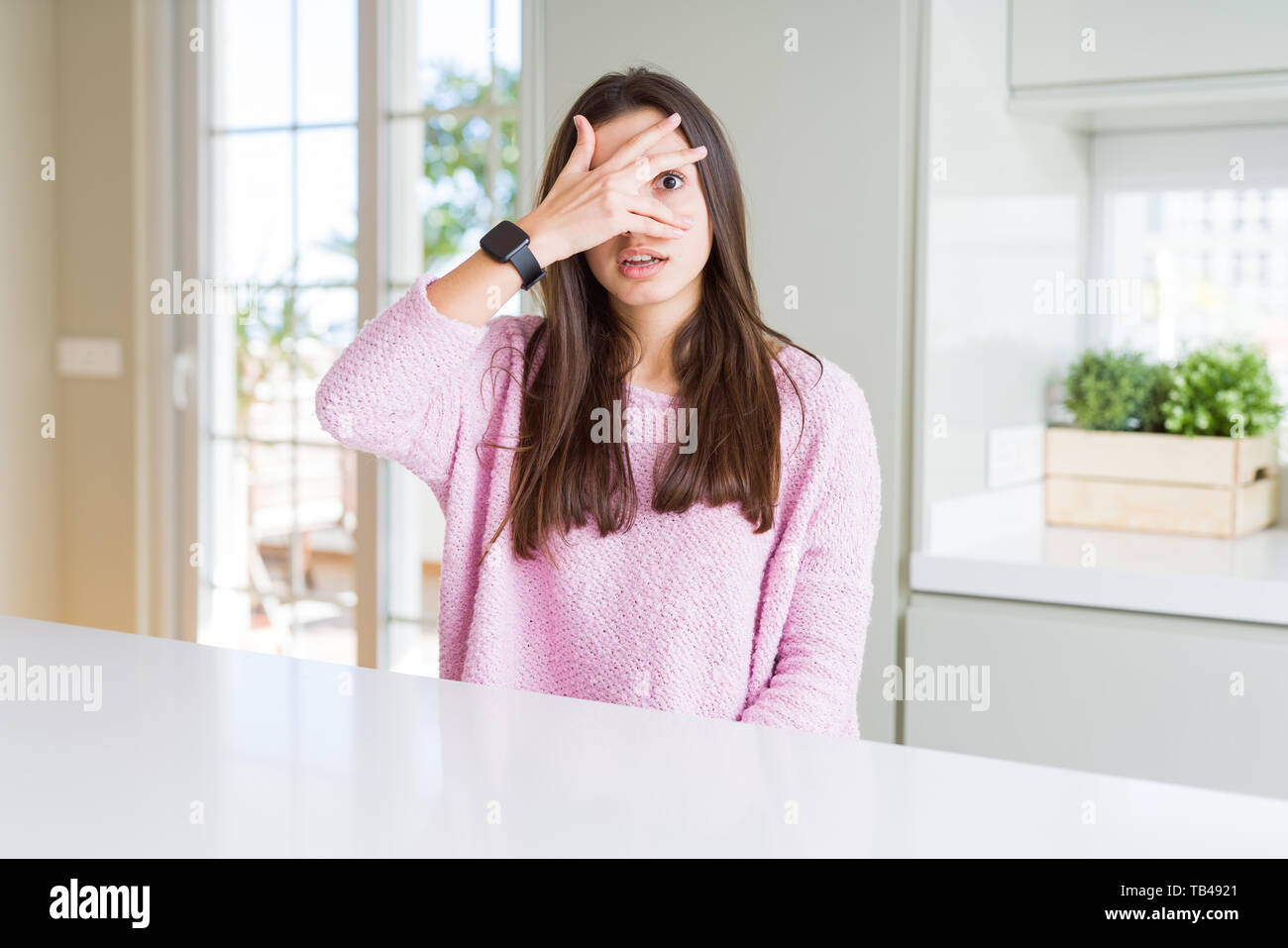 Beautiful young woman wearing pink sweater peeking in shock covering ...