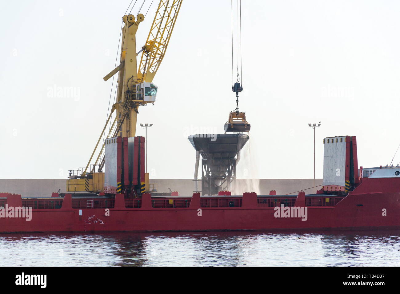 Yellow crane unloading sand from large freighter cargo ship in harbor ...
