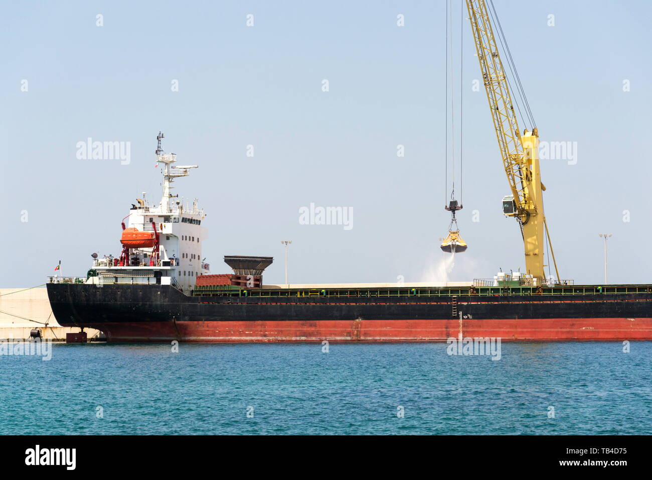 Yellow crane unloading sand from large freighter cargo ship in harbor ...