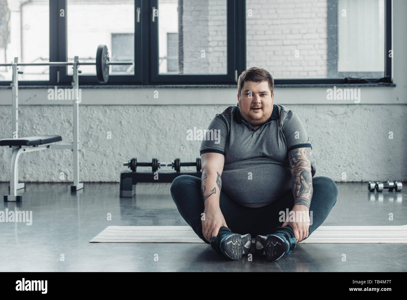 overweight tattooed man sitting and Looking At Camera during stretching ...