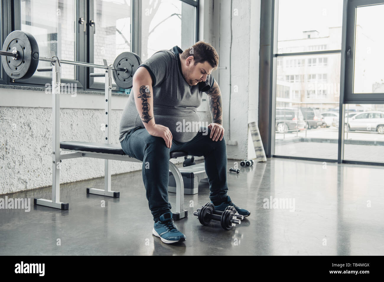 tired Overweight man sitting on bench after exercising with dumbbells ...