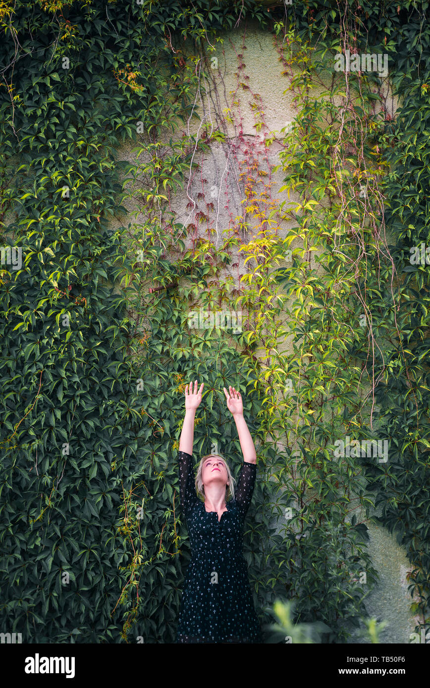 Young woman reaching upwards on foliage wall Stock Photo - Alamy