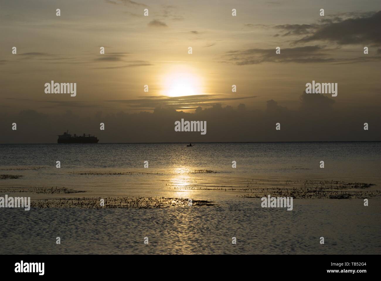 Dull gold colors of sunset with a silhouette of a ship in the distance ...