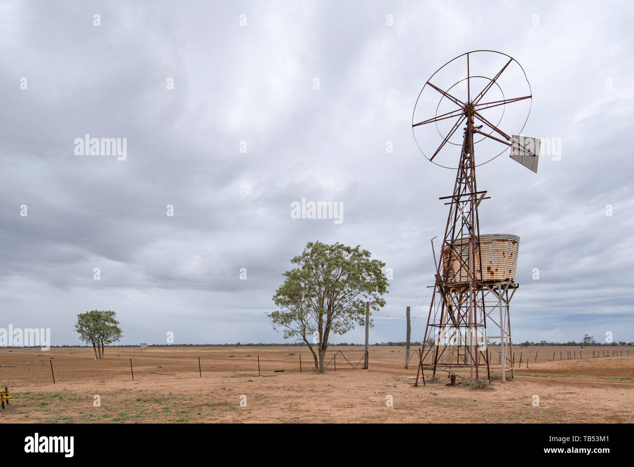 An old and unusable windmill and water tank on a stand in a dry and ...