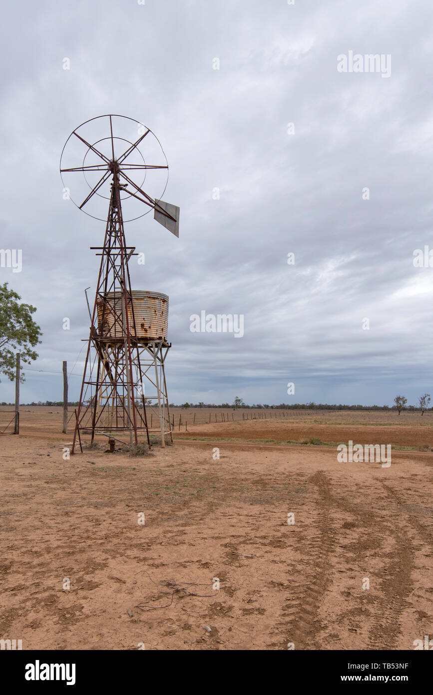 An old and unusable windmill and water tank on a stand in a dry and ...