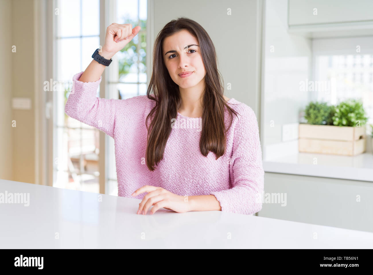 Beautiful young woman wearing pink sweater angry and mad raising fist ...