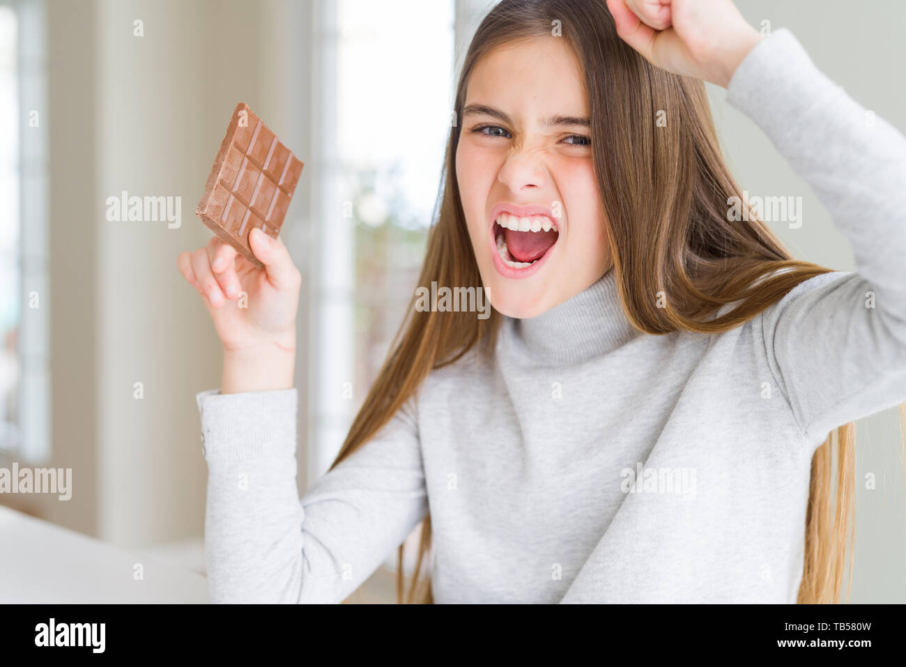 Beautiful young girl kid eating chocolate bar annoyed and frustrated ...