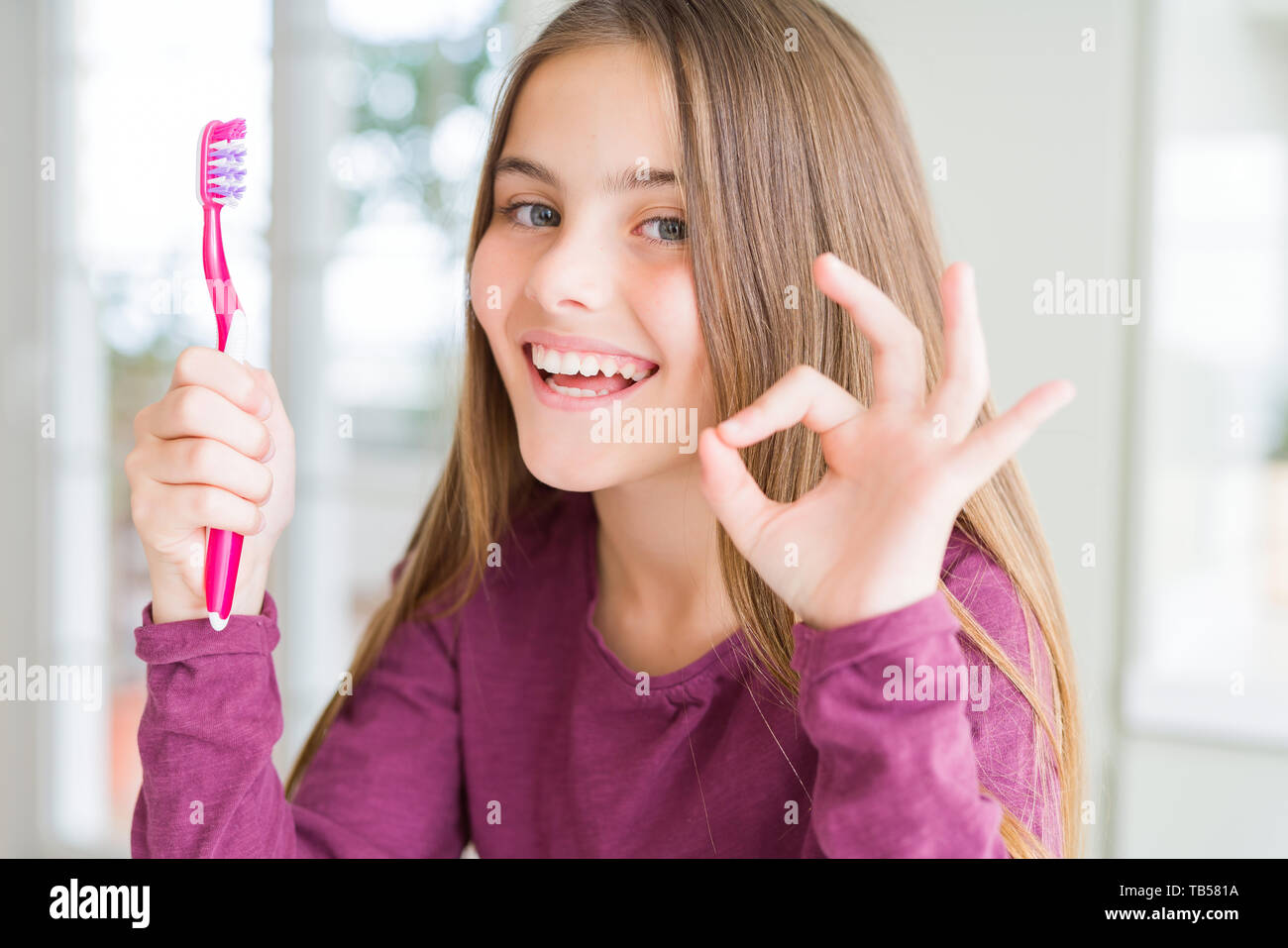 Beautiful young girl kid holding pink dental toothbrush doing ok sign ...