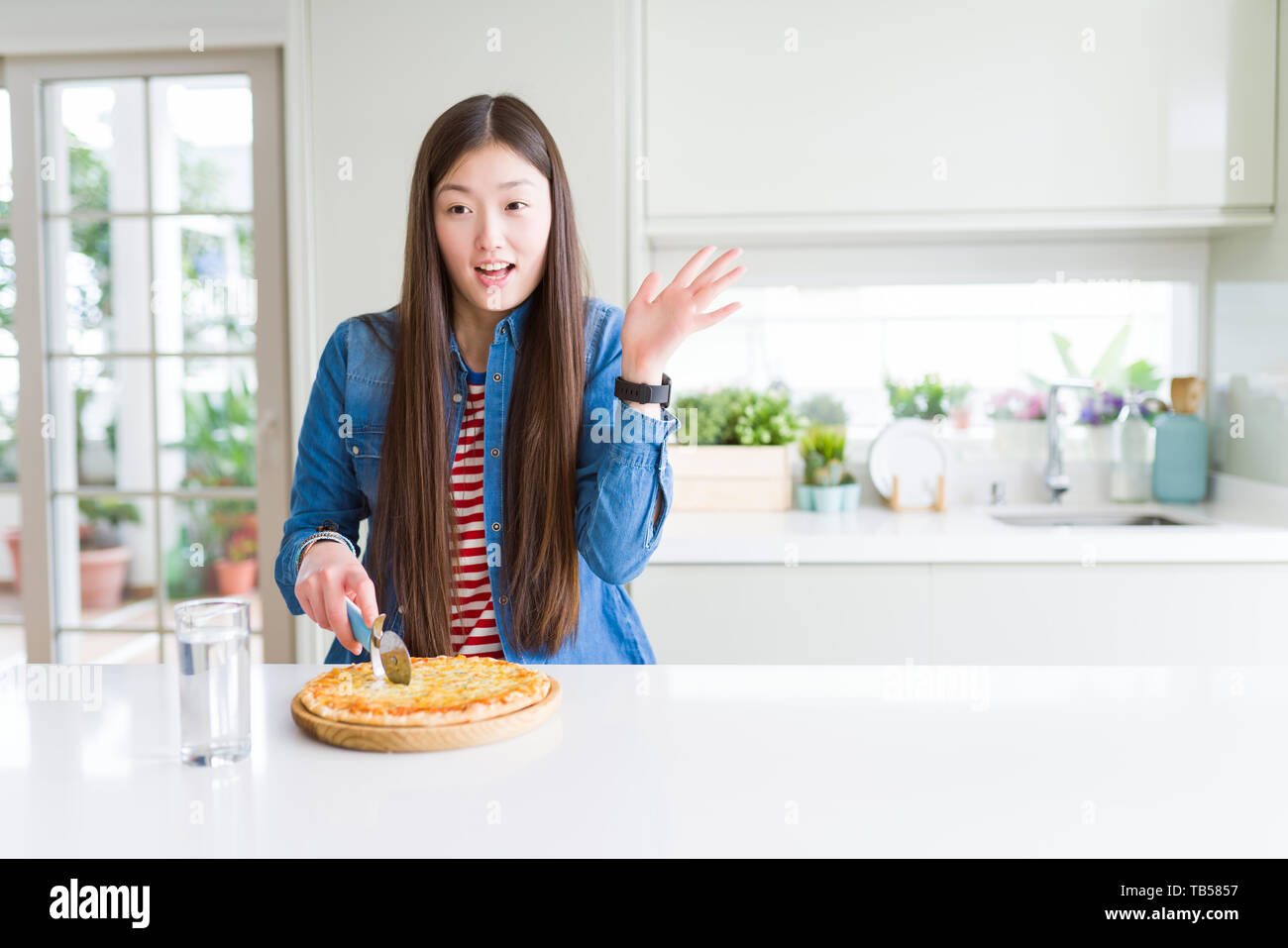 Beautiful Asian woman eating and cutting chesse pizza very happy and excited, winner expression ...