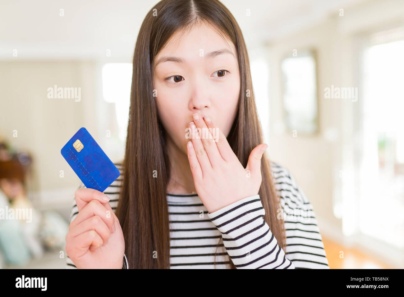 Beautiful Asian woman holding credit card cover mouth with hand shocked ...