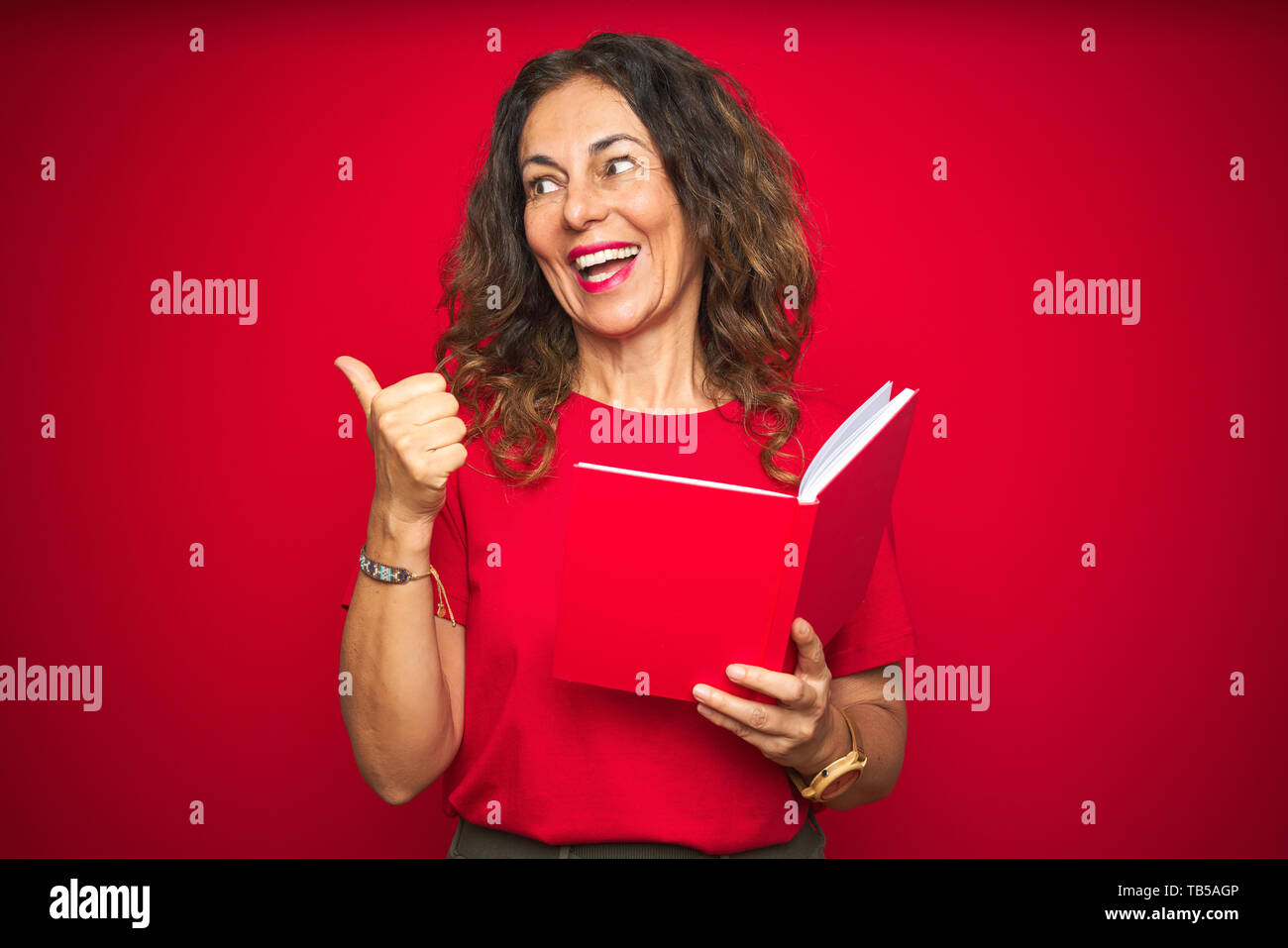 Middle age senior woman reading a book over red isolated background ...