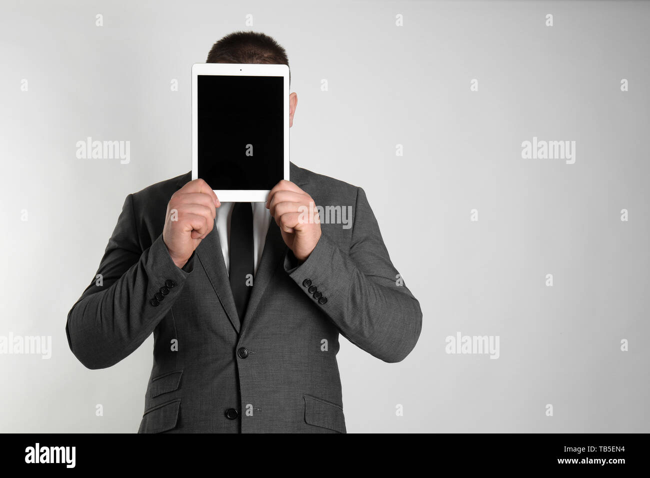 Businessman hiding face behind tablet computer on light background ...