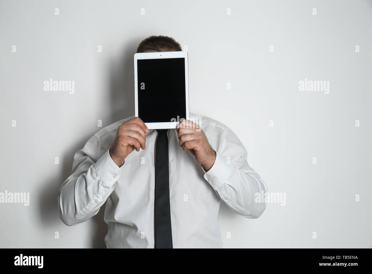 Businessman hiding face behind tablet computer on light background ...