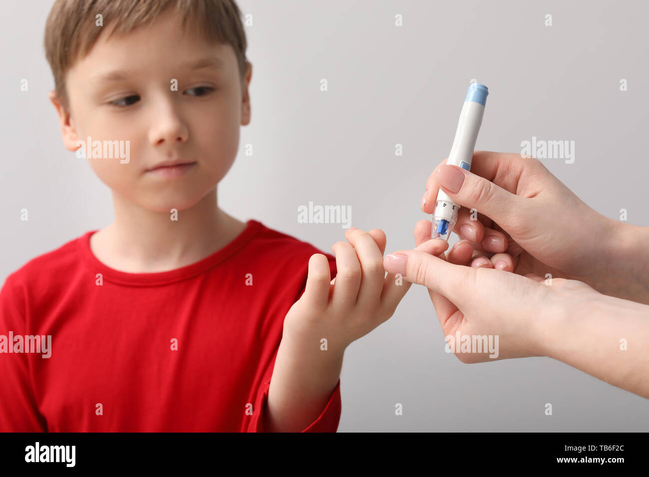 Mother taking blood sample of her diabetic child with lancet pen on ...