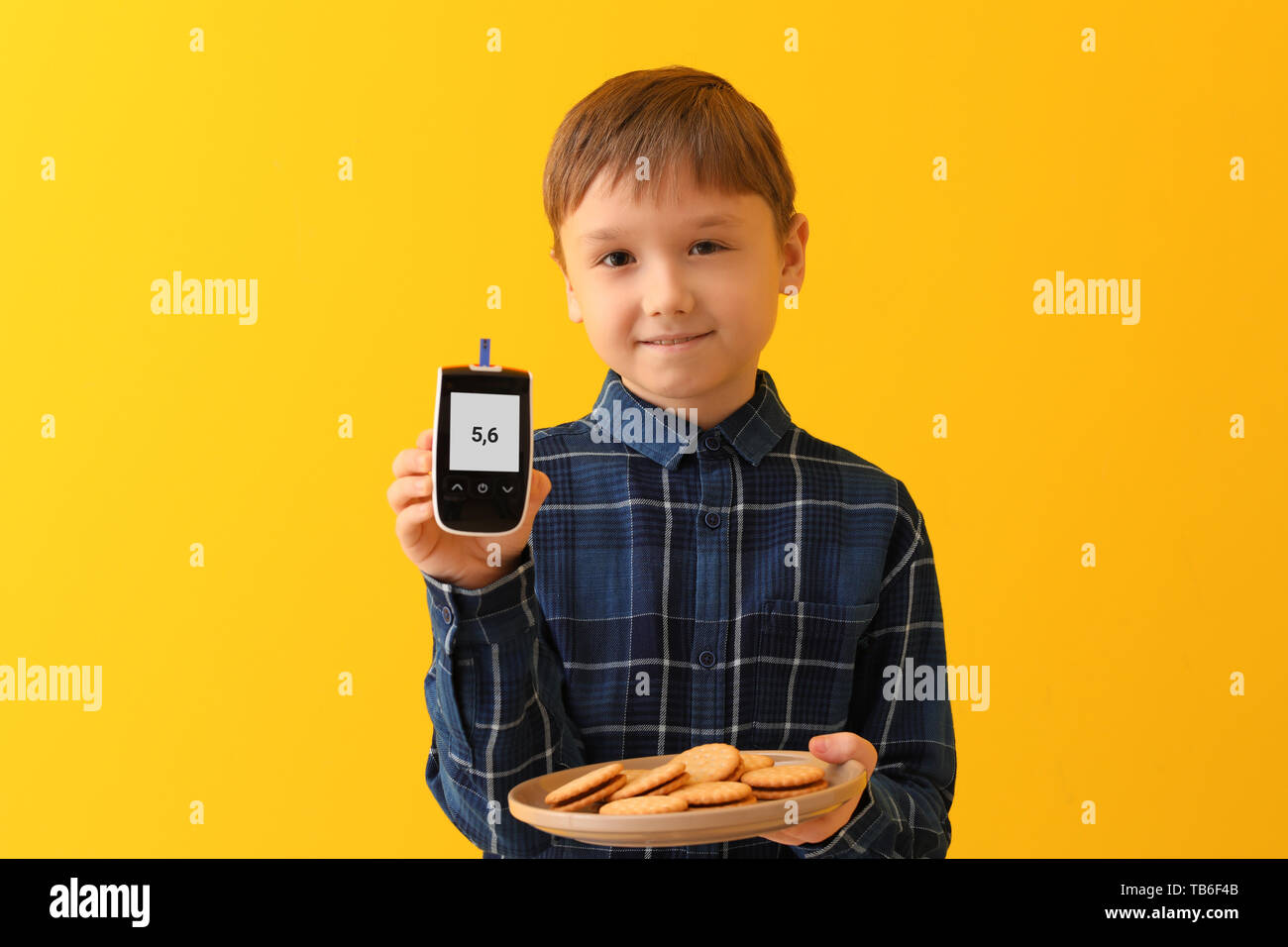 Diabetic child with digital glucometer and cookies on color background ...