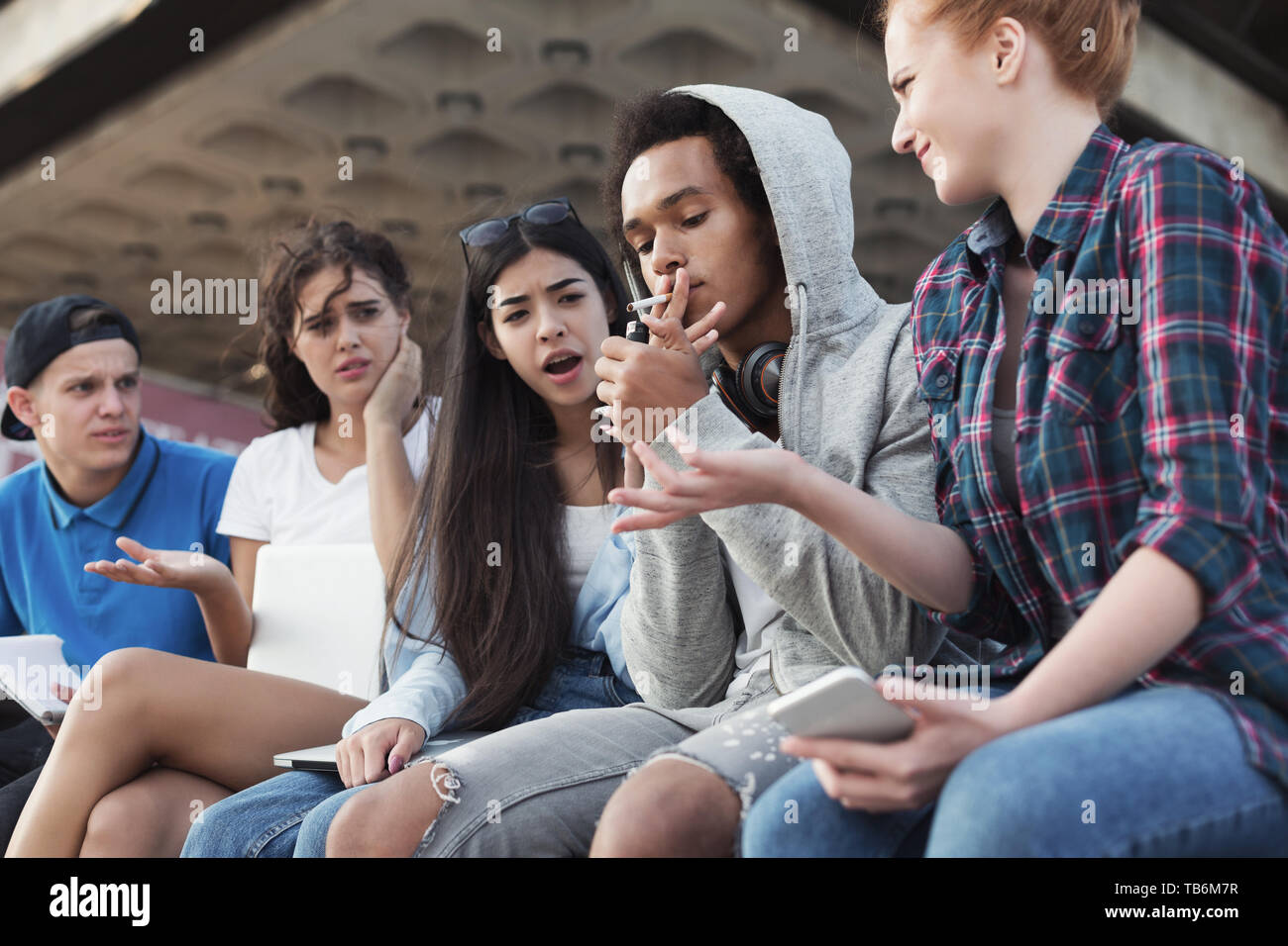Black teen guy smoking cigarette, his friends judging him. Social ...