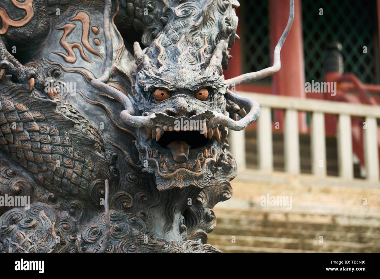 A fierce bronze dragon statue stands in front of the steps leading up ...