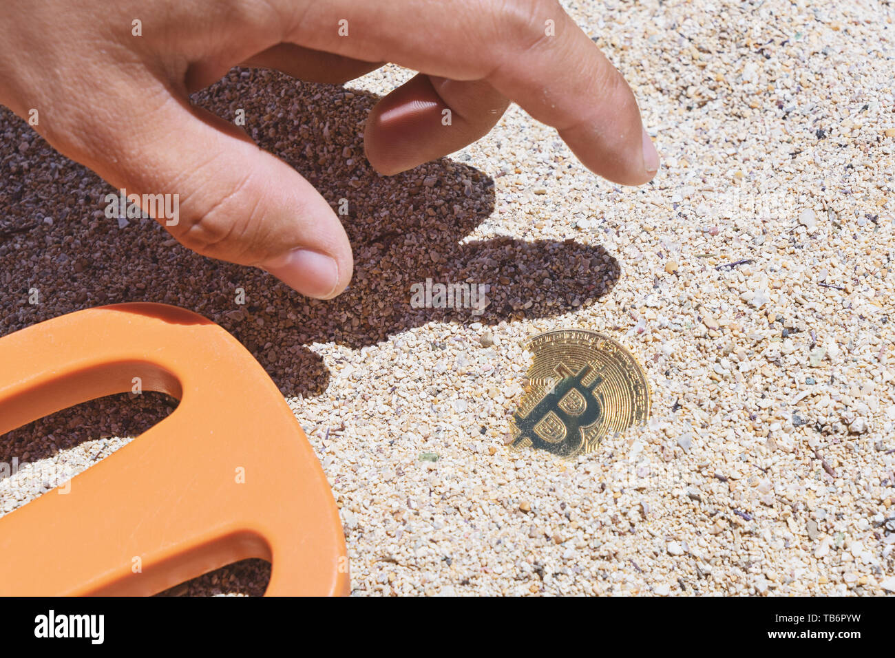 Closeup of a symbolic bitcoin coin on the sand in man hand. The concept ...