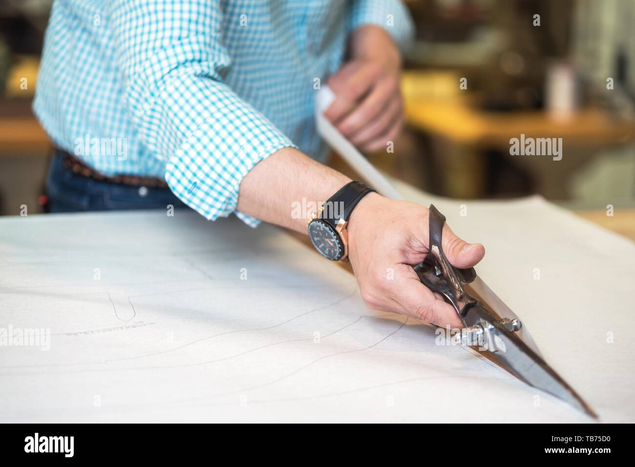 Tailor cutting out the marked pattern on fabric with large scissors on ...