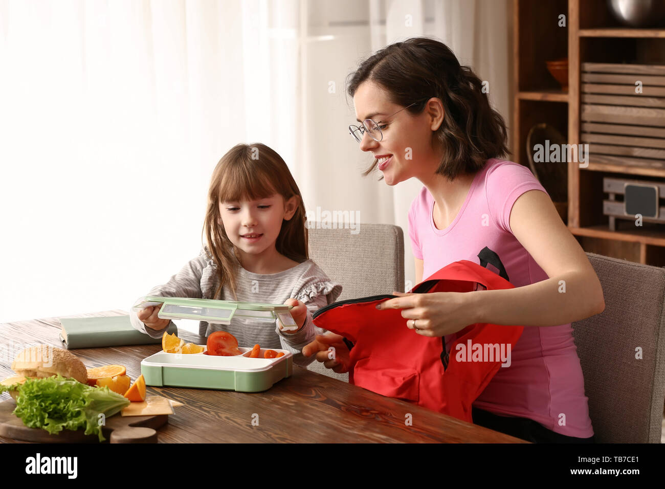 Mother with cute daughter packing lunch box into backpack at home Stock ...