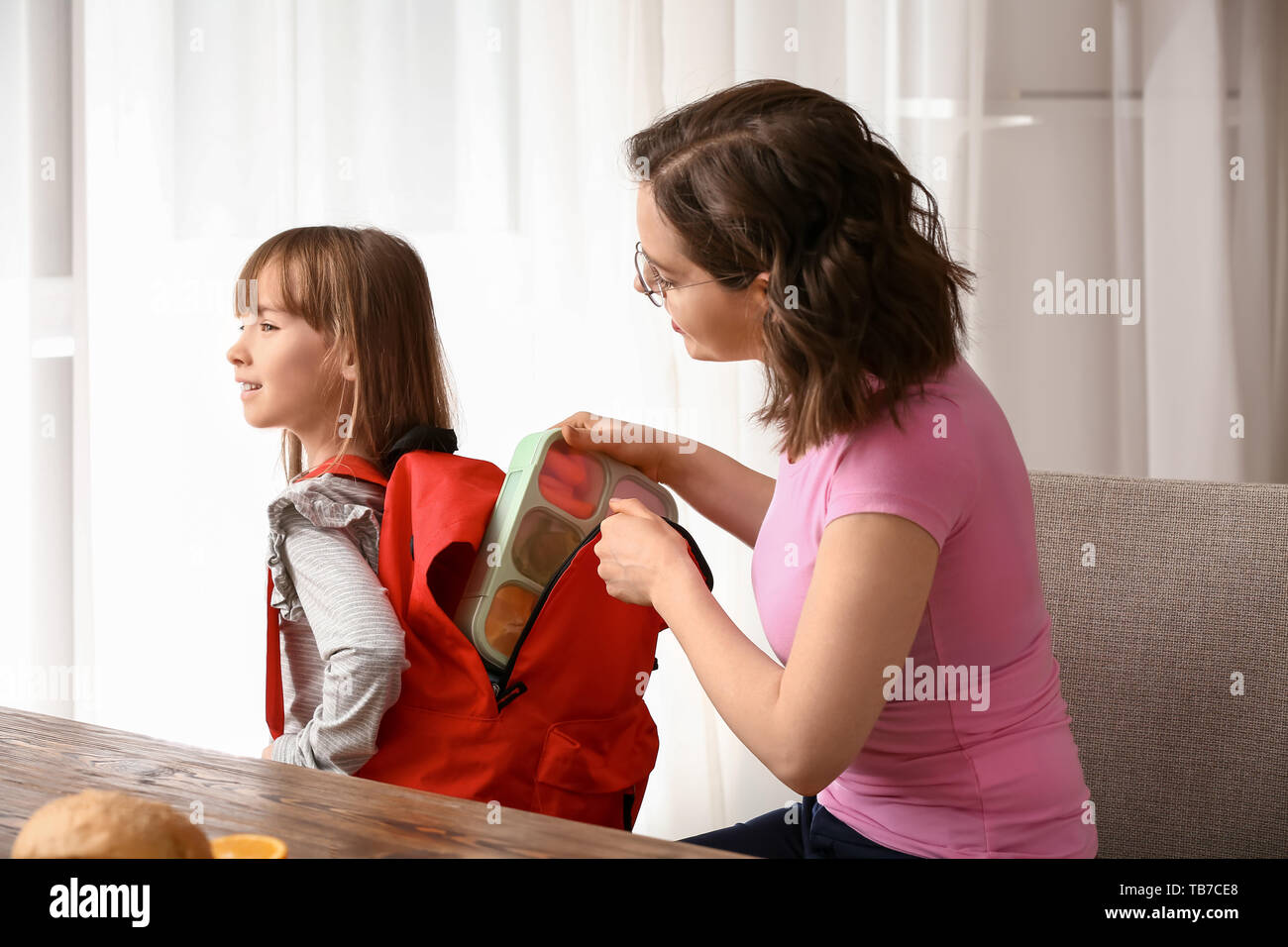 Mother packing lunch box into backpack of cute daughter at home Stock ...