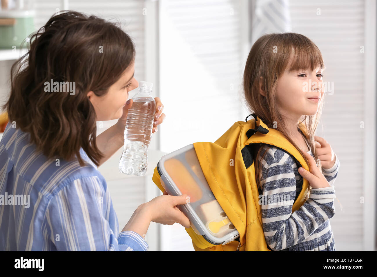 Mother packing lunch box into backpack of cute daughter at home Stock ...