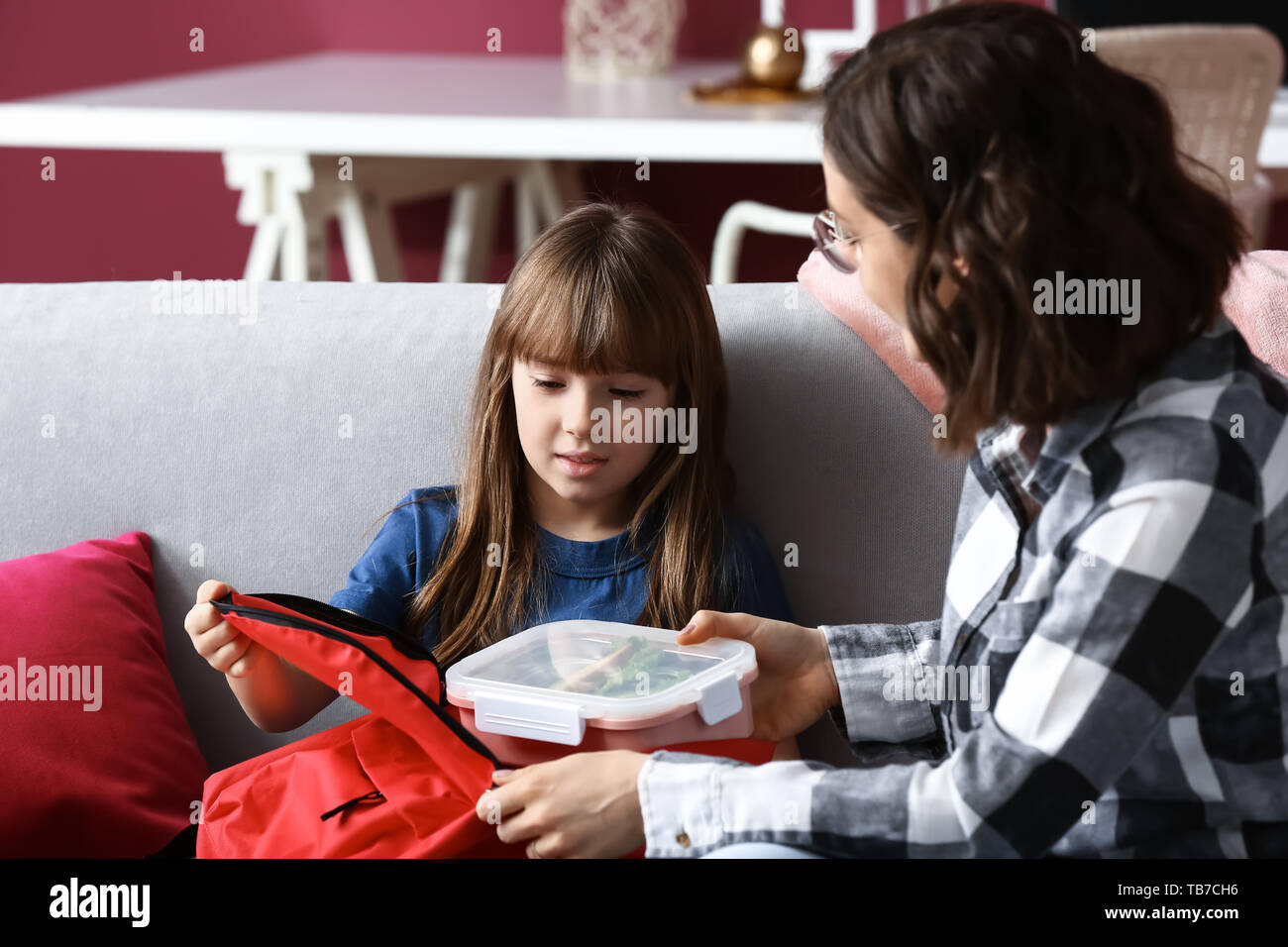 Mother with cute daughter packing lunch box into backpack at home Stock ...