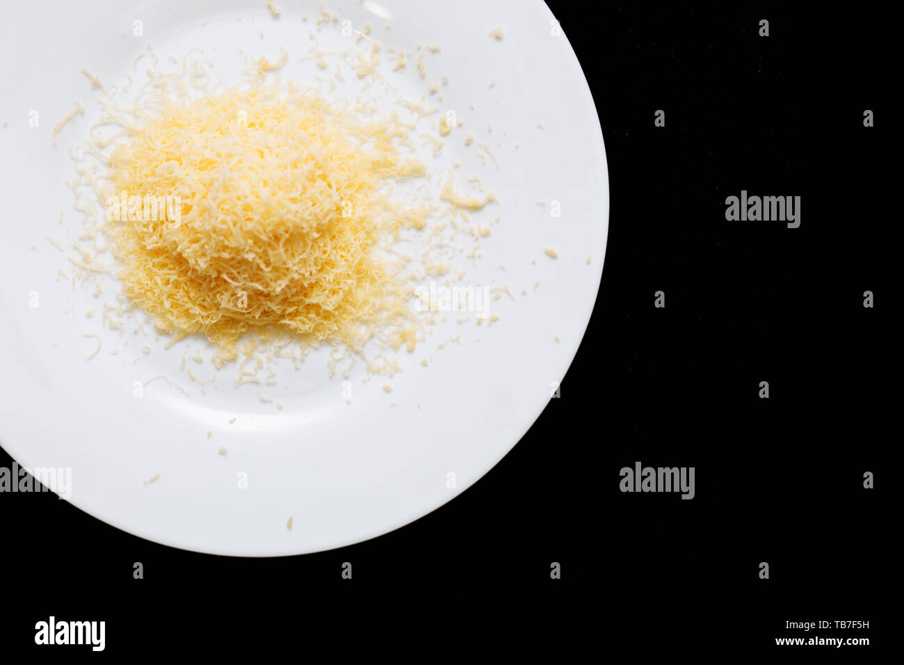 Shredded grated cheese in a large white ceramic plate on a black ...