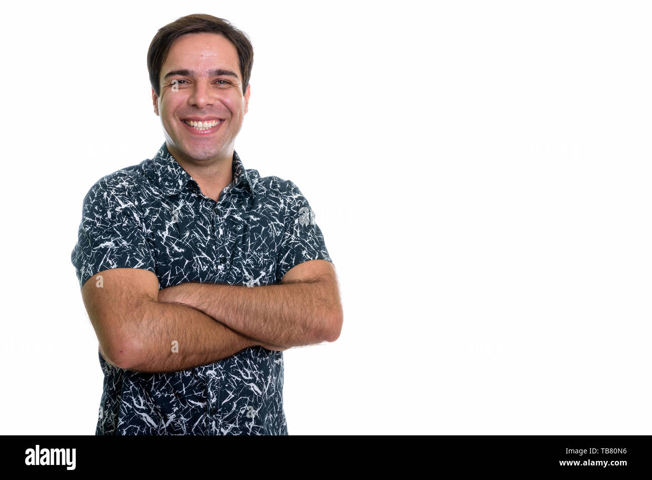 Studio shot of young happy Persian man smiling with arms crossed ...