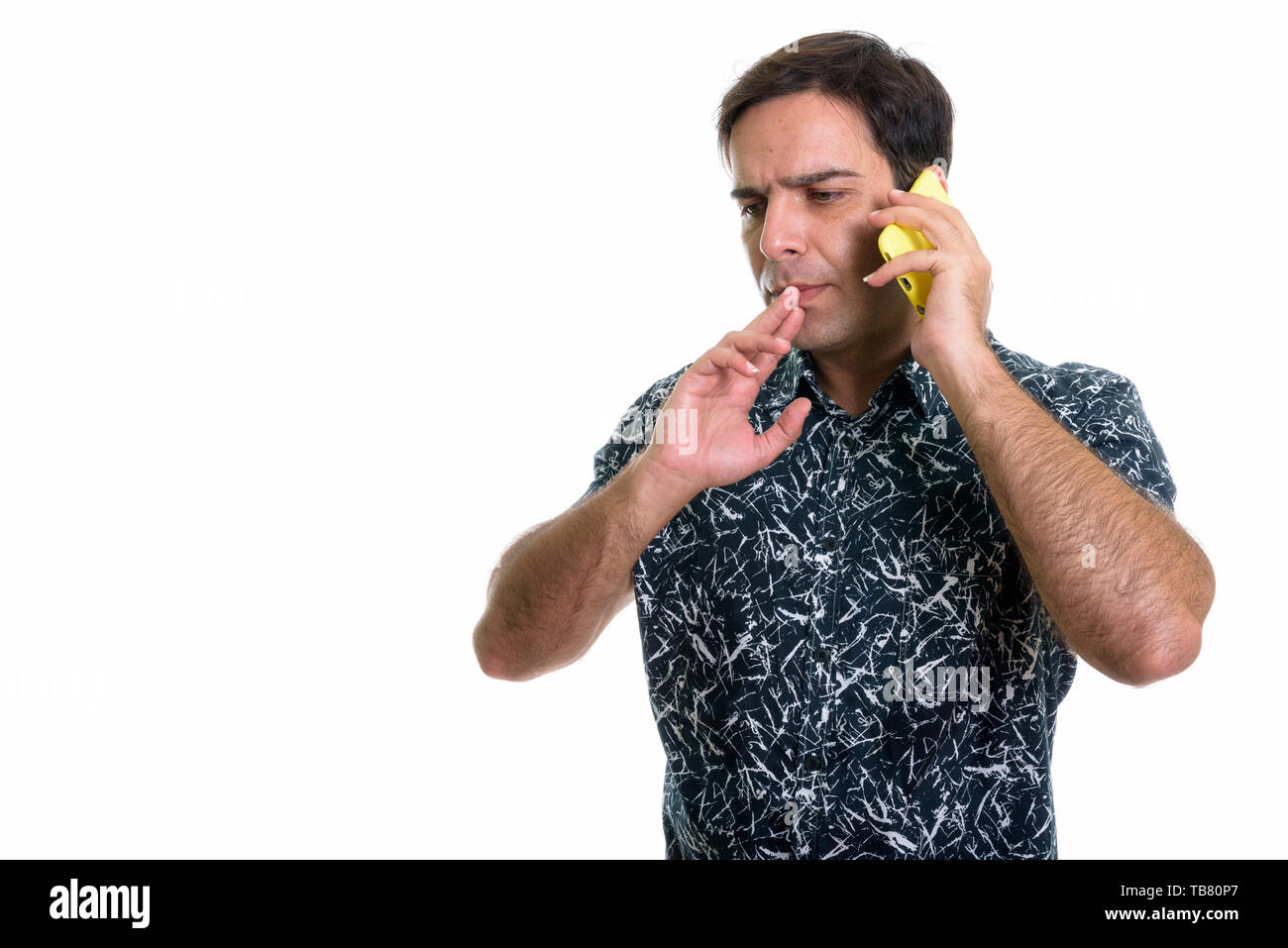 Studio shot of young Persian man thinking while talking on mobile phone ...
