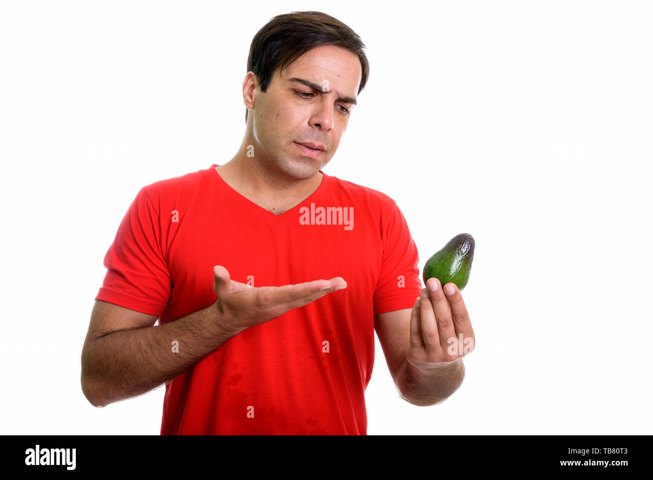 Studio shot of young Persian man looking and pointing at avocado ...