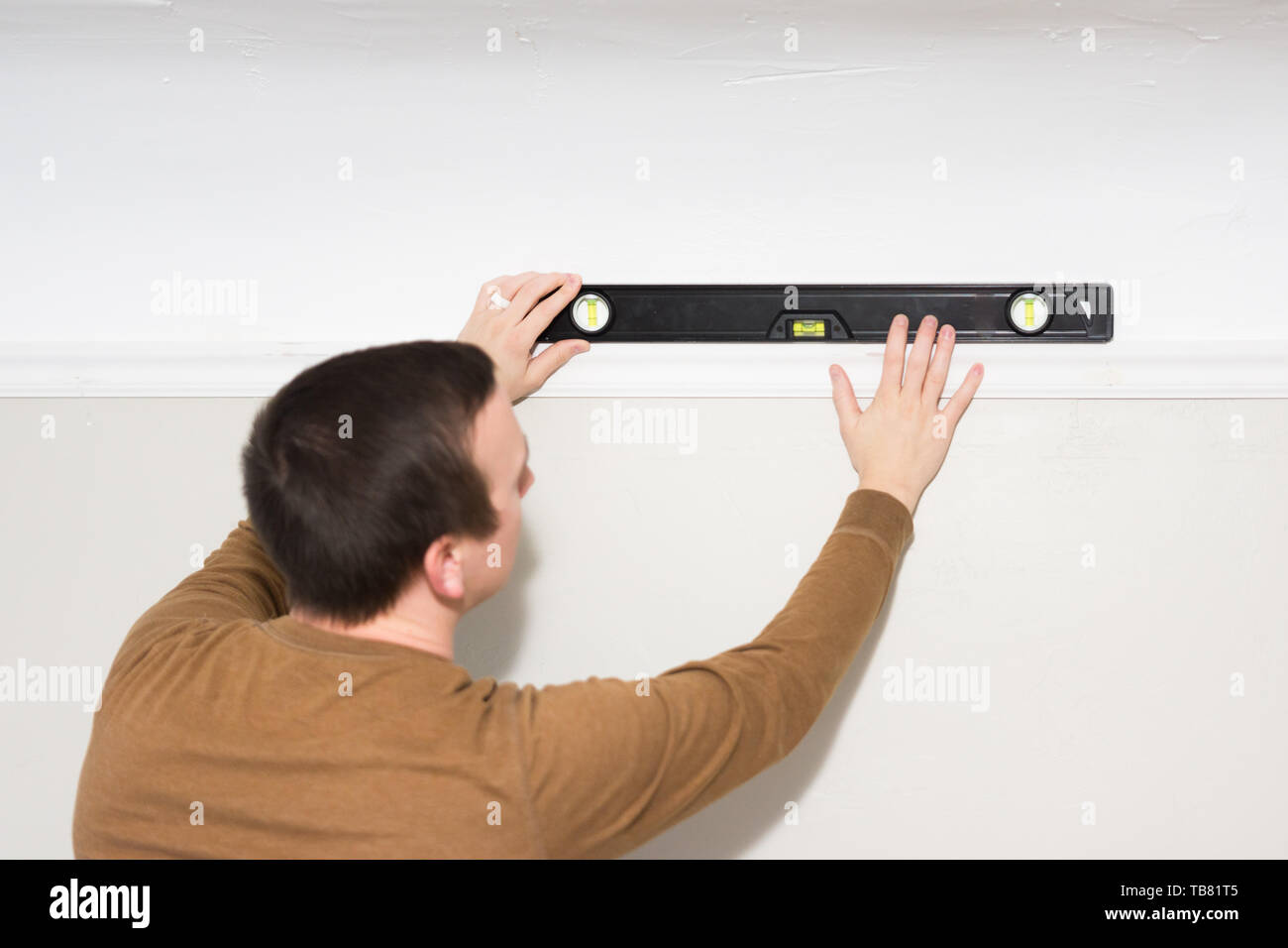 Caucasian man uses bubble level to level white wood trim crown moulding ...