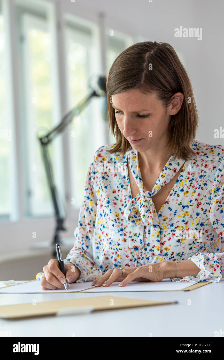 Young businesswoman or secretary sitting at her office desk writing ...