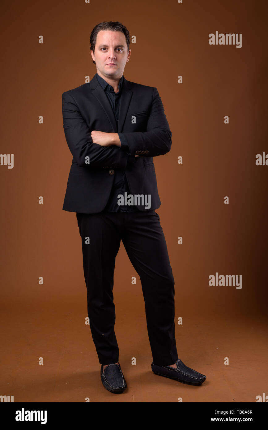 Studio shot of Italian businessman wearing black suit against brown ...