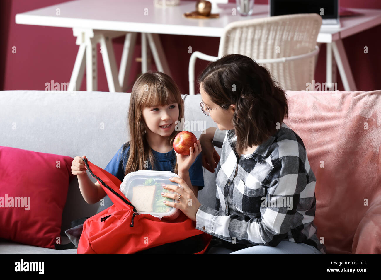 Mother with cute daughter packing lunch box into backpack at home Stock ...