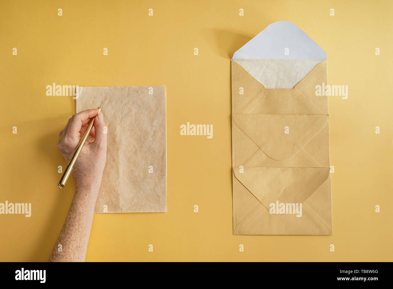 Female hand writing letter and paper envelopes on color background ...