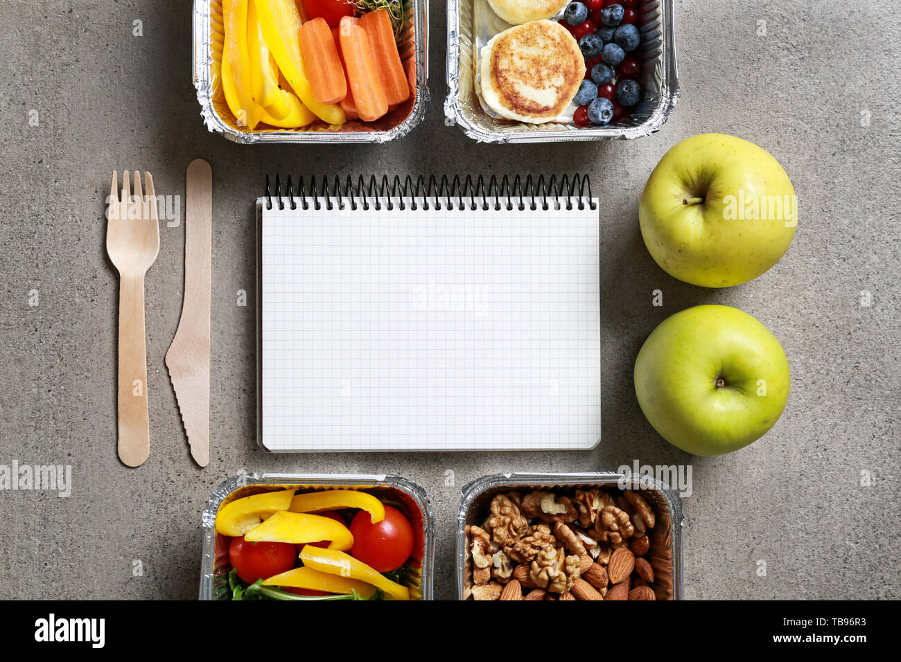 Containers with delicious food and blank notebook on grey background ...