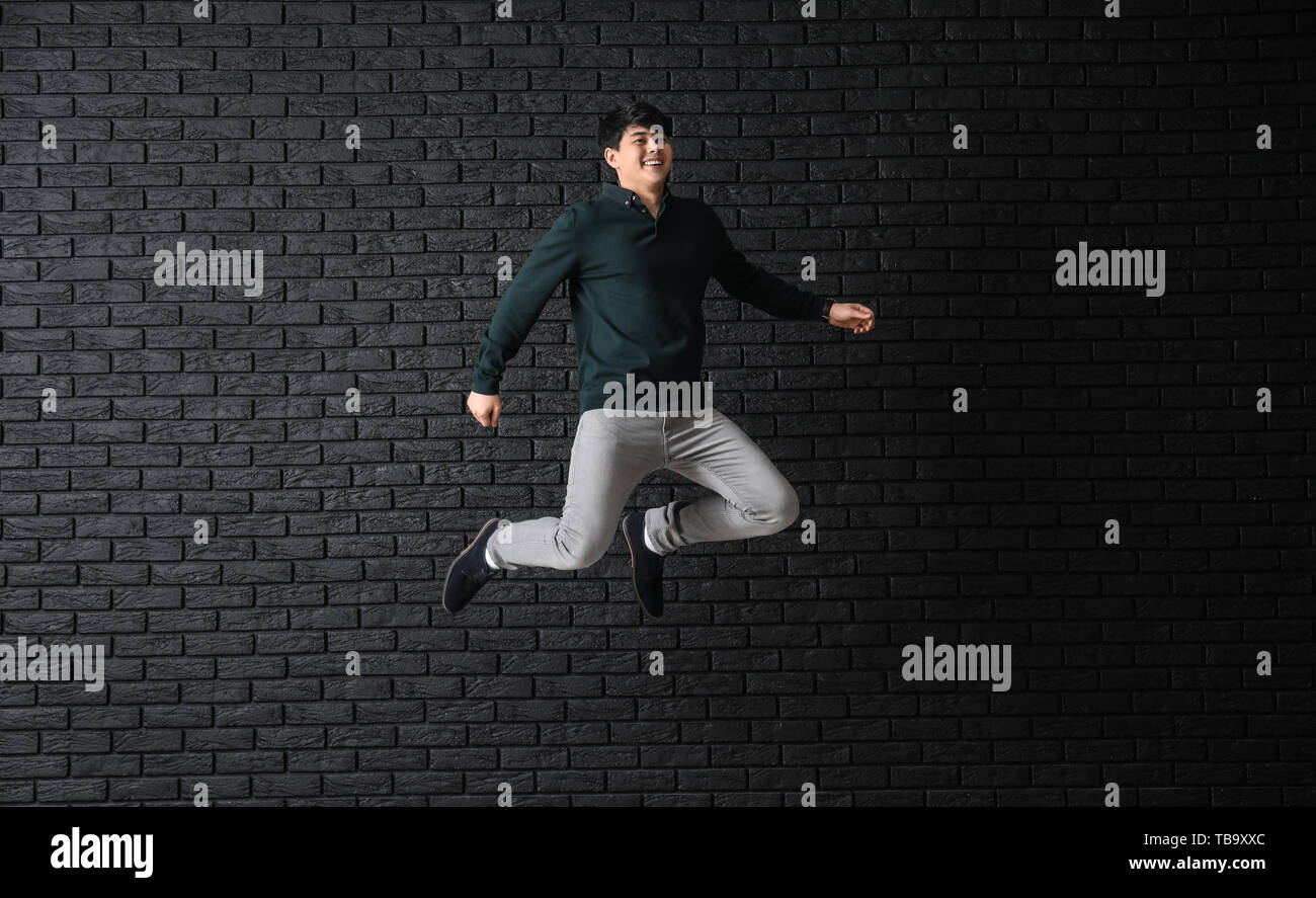 Jumping Asian man against dark brick background Stock Photo - Alamy