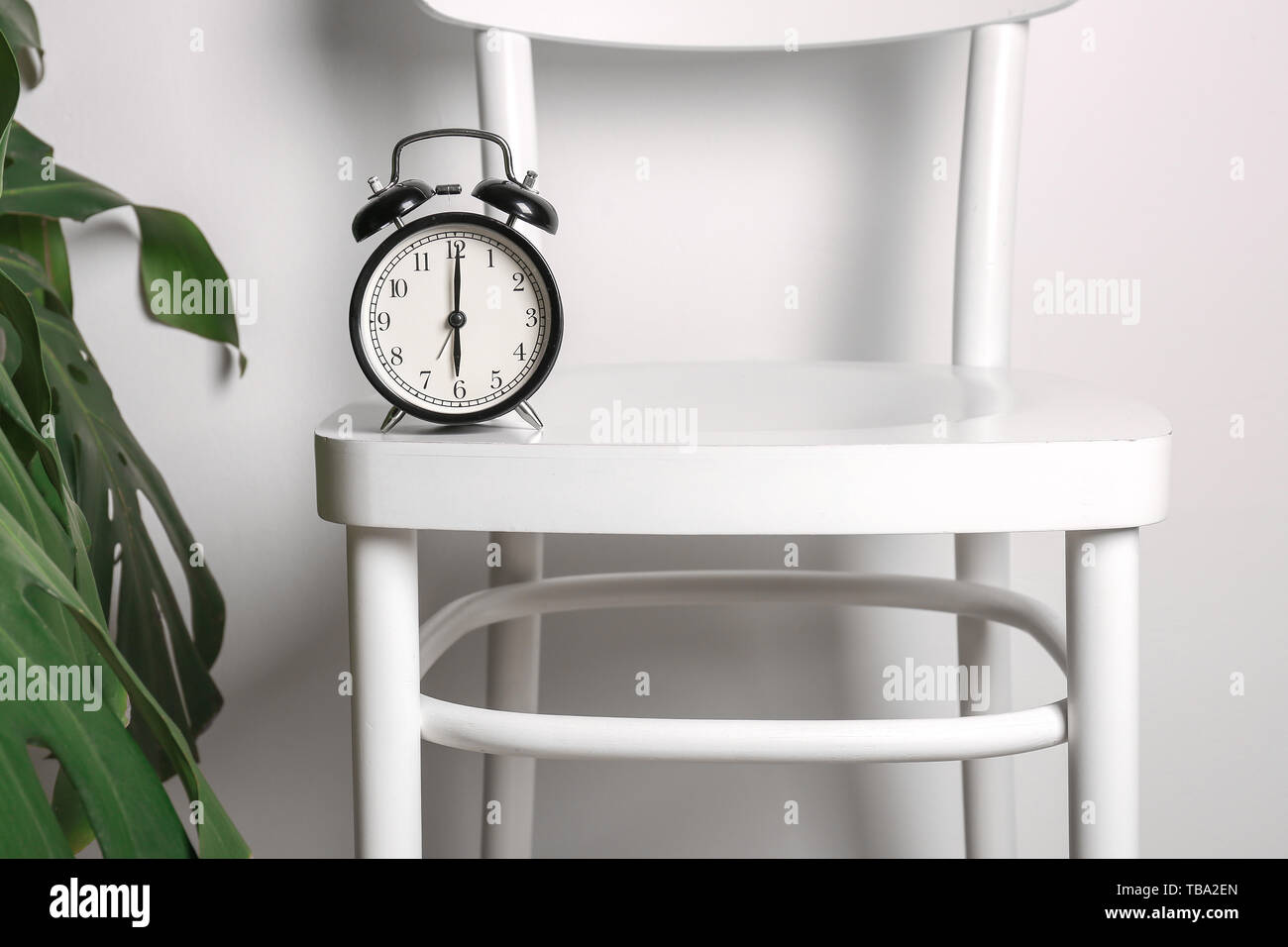 Alarm clock on chair against white background Stock Photo - Alamy