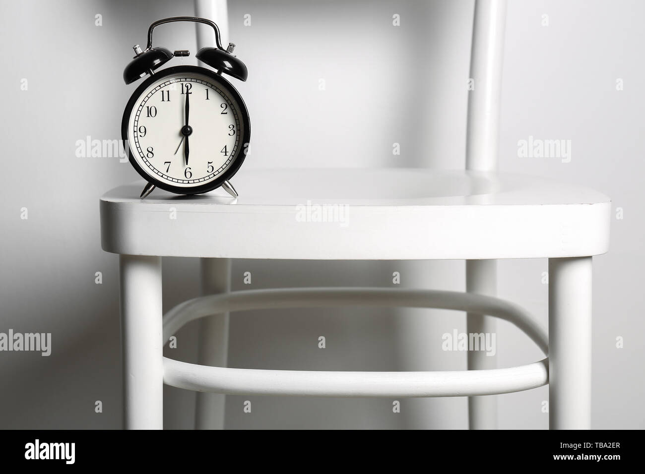 Alarm clock on chair against white background Stock Photo - Alamy