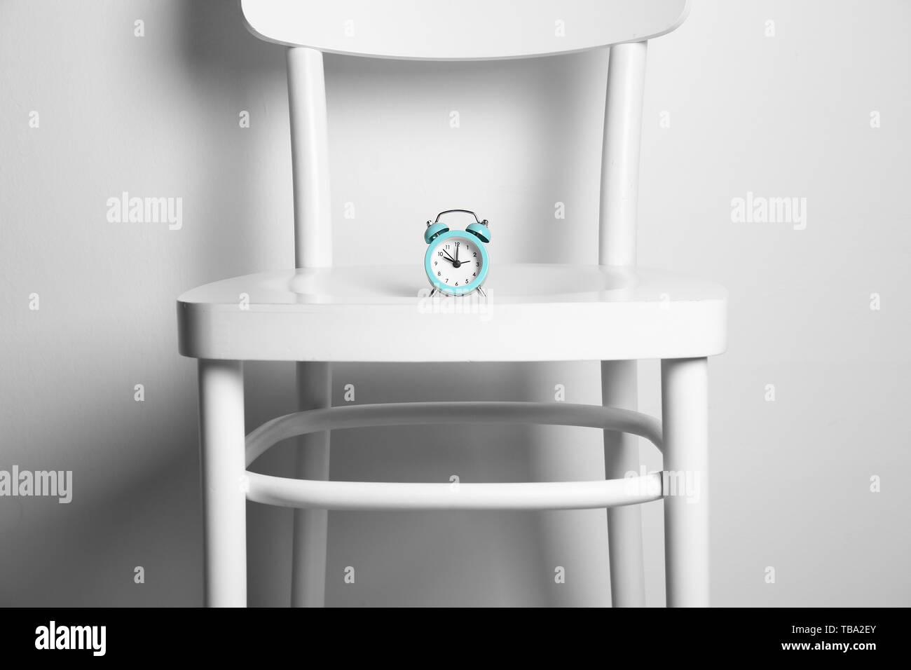 Alarm clock on chair against white background Stock Photo - Alamy